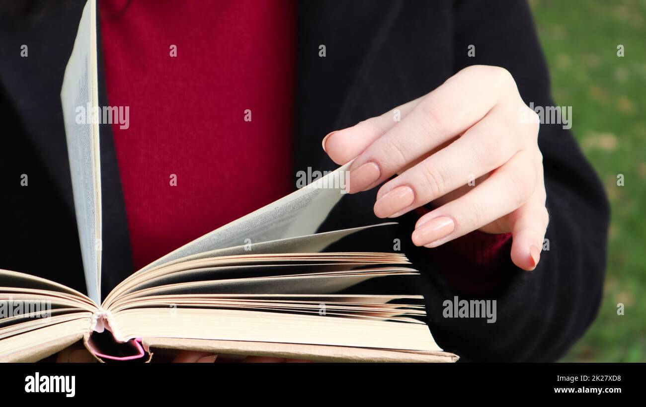 Girl reading a book in the park. Female hands flipping pages of paper ...
