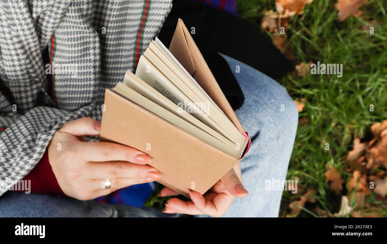 Girl reading a book in the autumn park. Female hands open the pages of ...