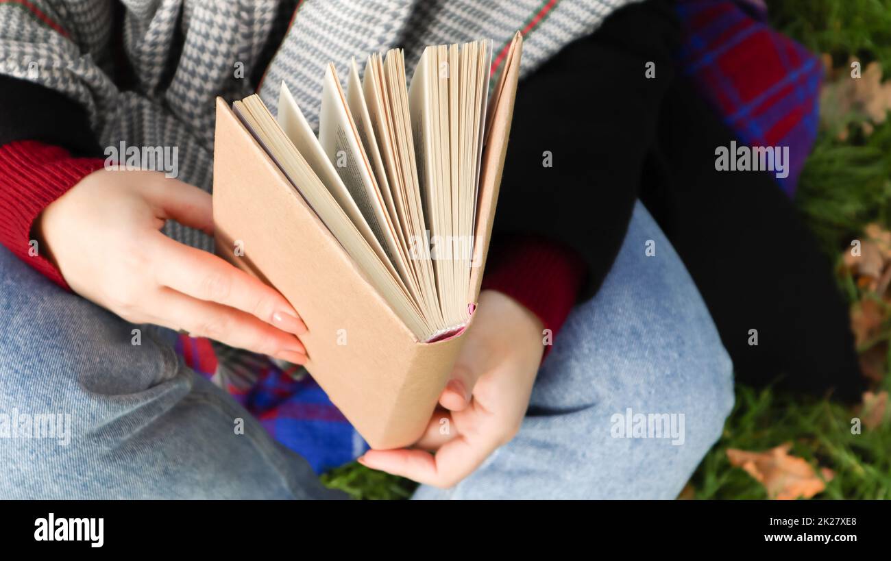Girl reading a book in the autumn park. Female hands open the pages of ...
