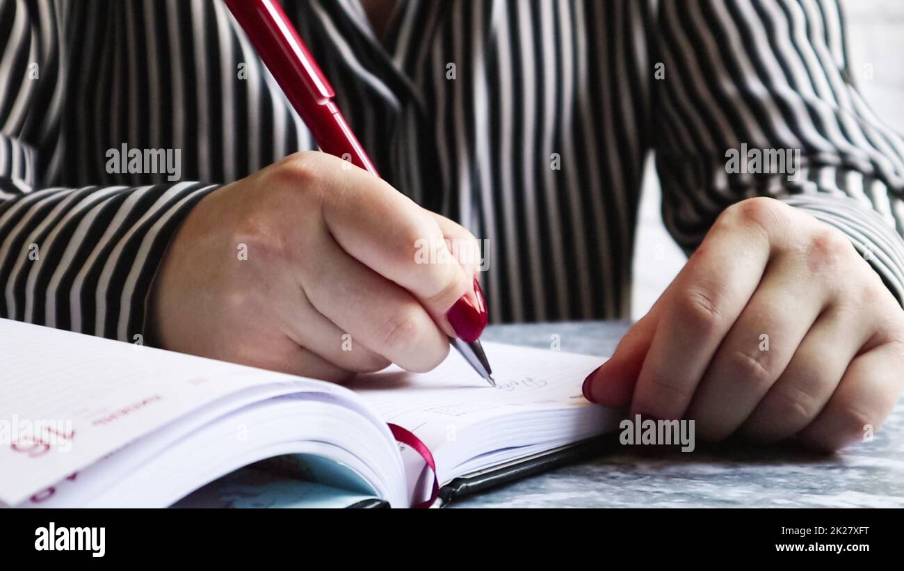 Side view of the hands of a woman with red nails, holding a red pen ...