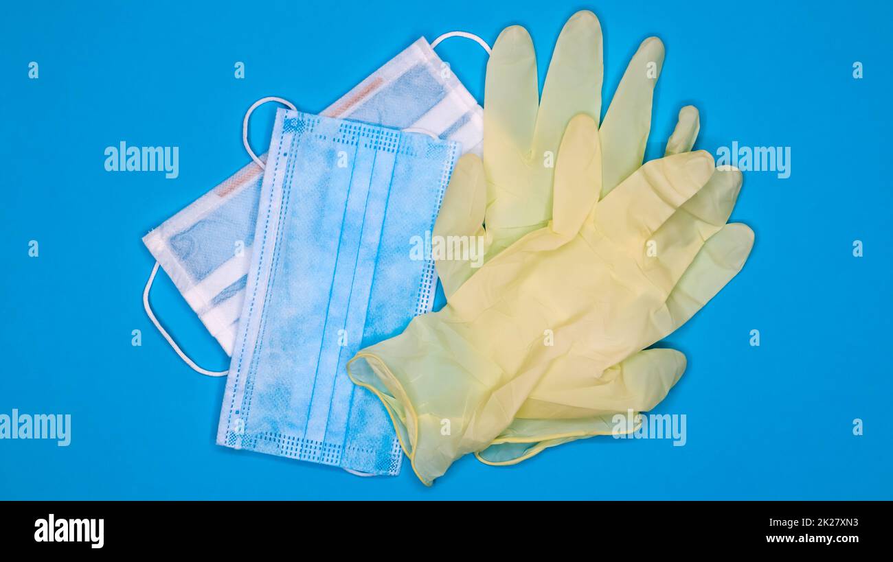 A pair of disposable latex medical gloves and a surgical mask on a blue ...