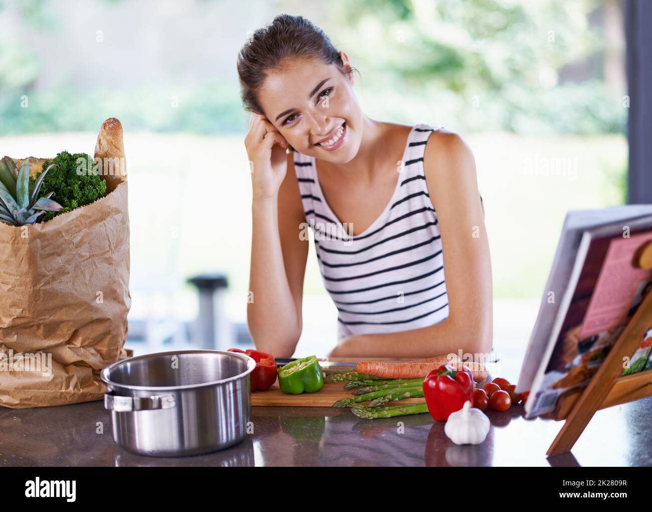 Living life the healthy way. A young woman cooking from a recipe book ...