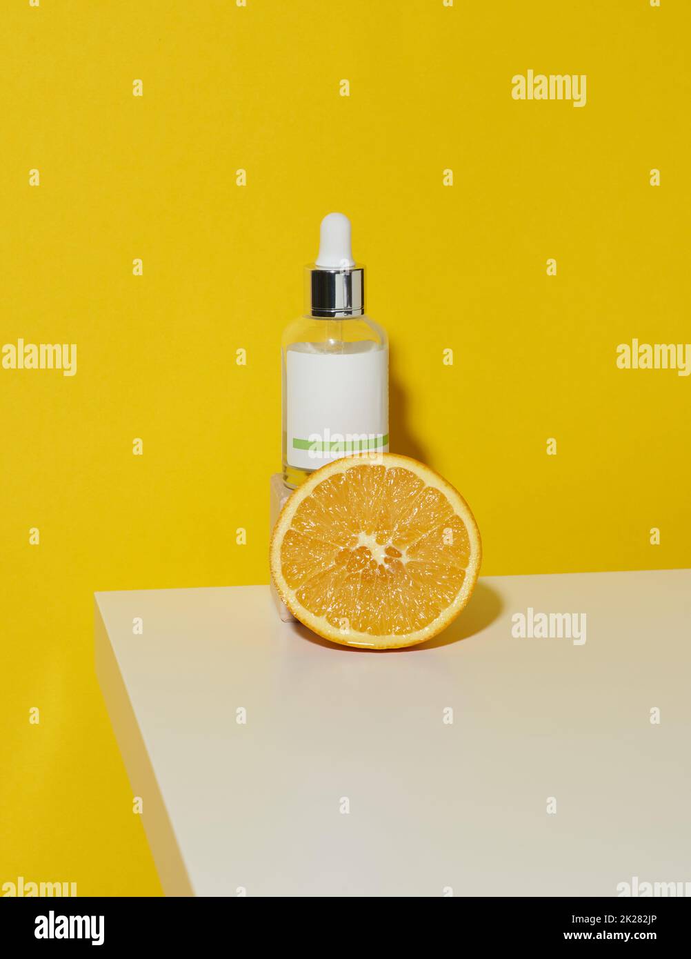 white glass bottle with a pipette and half an orange on a white surface ...