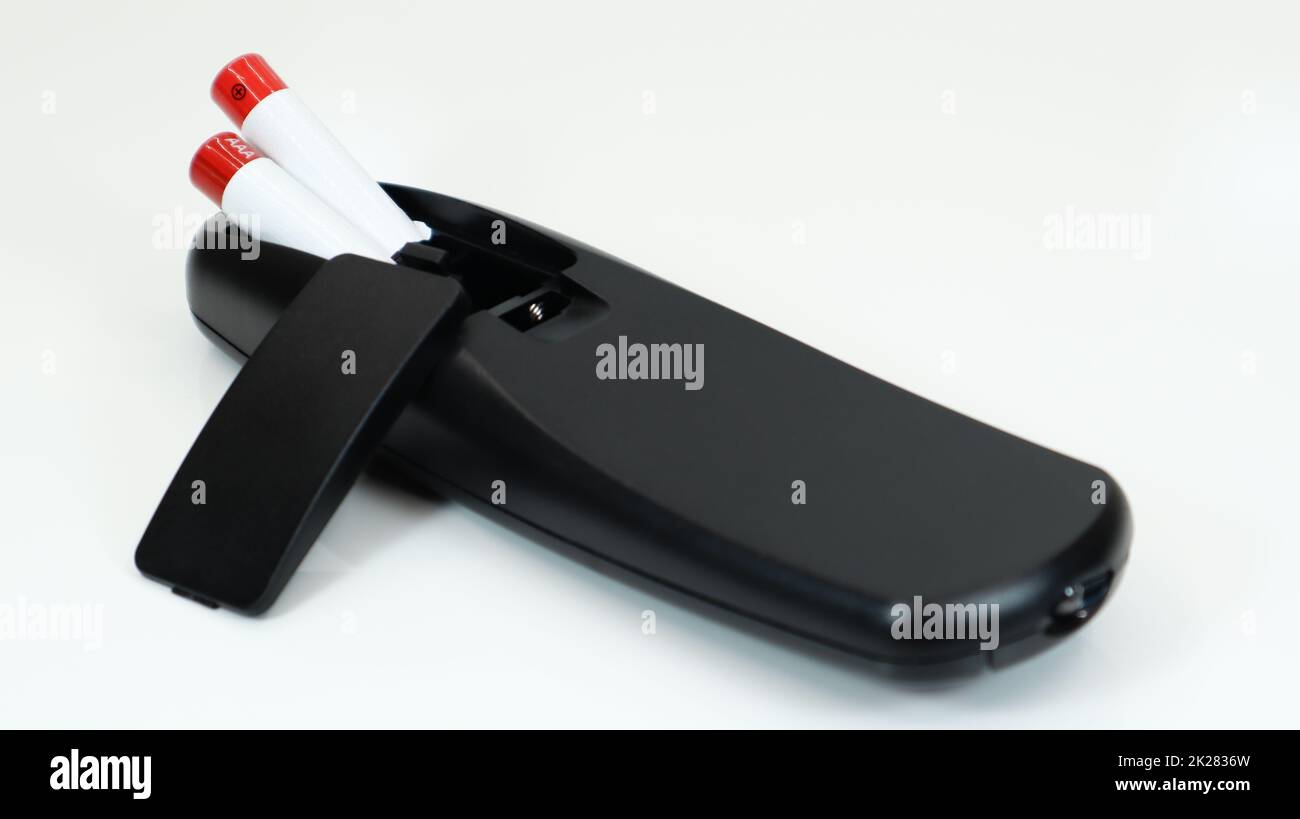 Black TV remote control with AAA alkaline batteries on a white ...