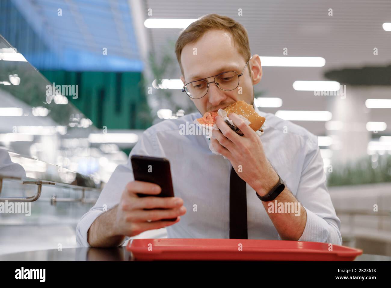 Office worker snacking on burger in mall, surfing the internet in a ...