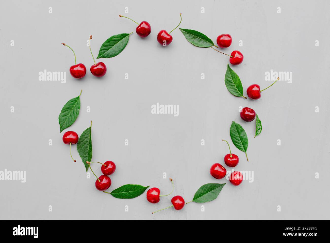 Gray flat lay with circle shape of big sweet cherry berries and leaves ...