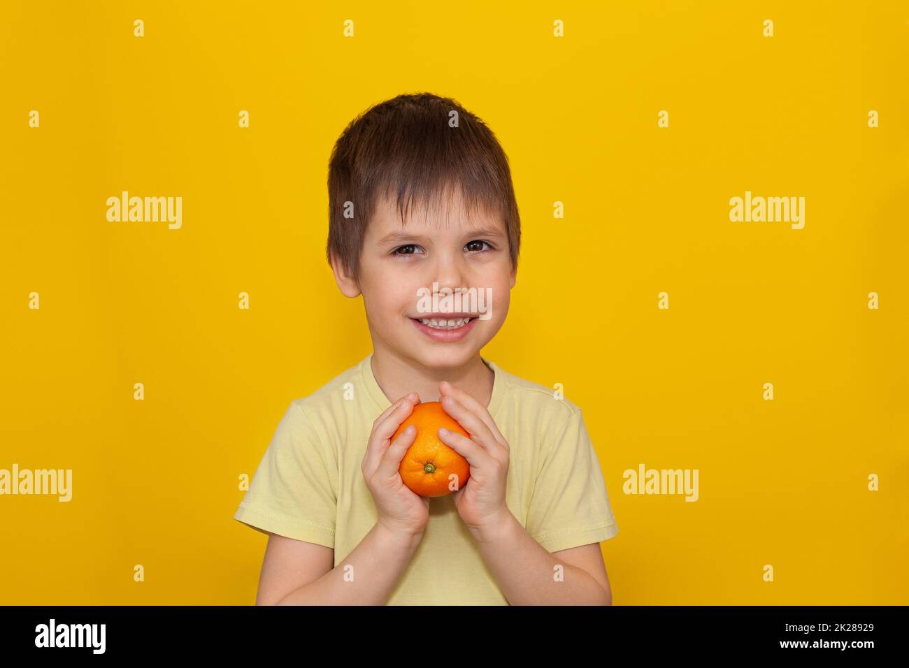 A cheerful child in a yellow T-shirt on a yellow background holds an ...