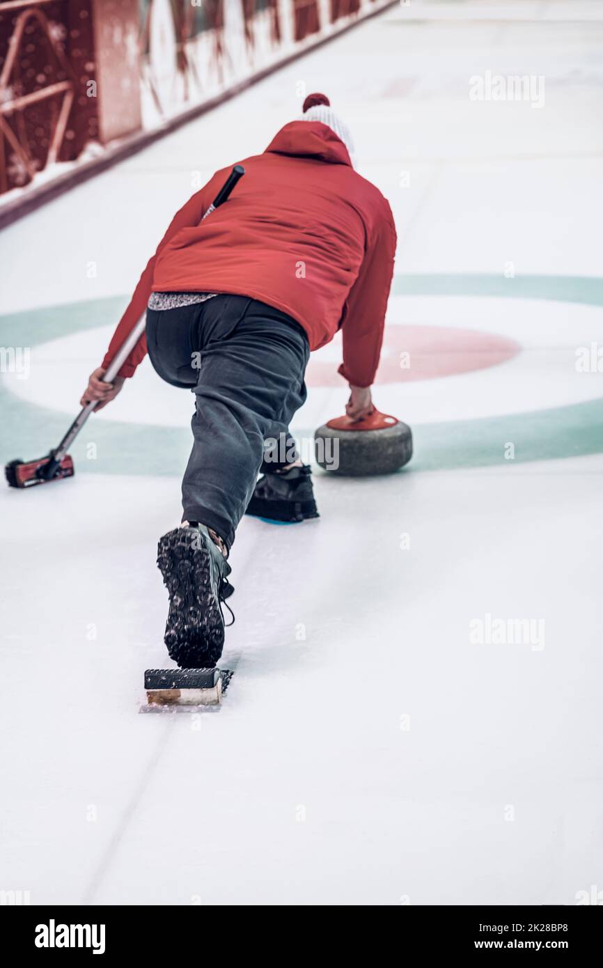 Curling game. Rear view of player playing curling on ice rink with ...