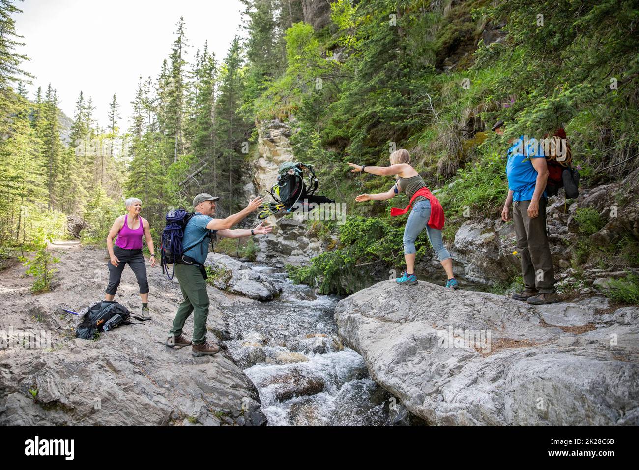 Woman throwing hiking backpack to man over stream in woods Stock Photo ...