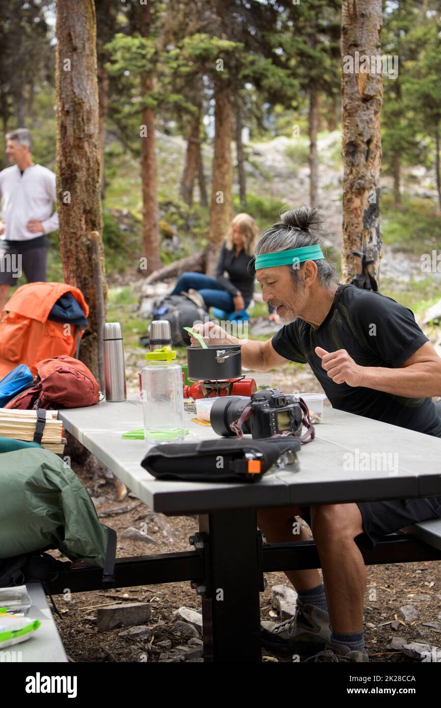 Man cooking at camping stove on picnic table at campsite in woods Stock ...