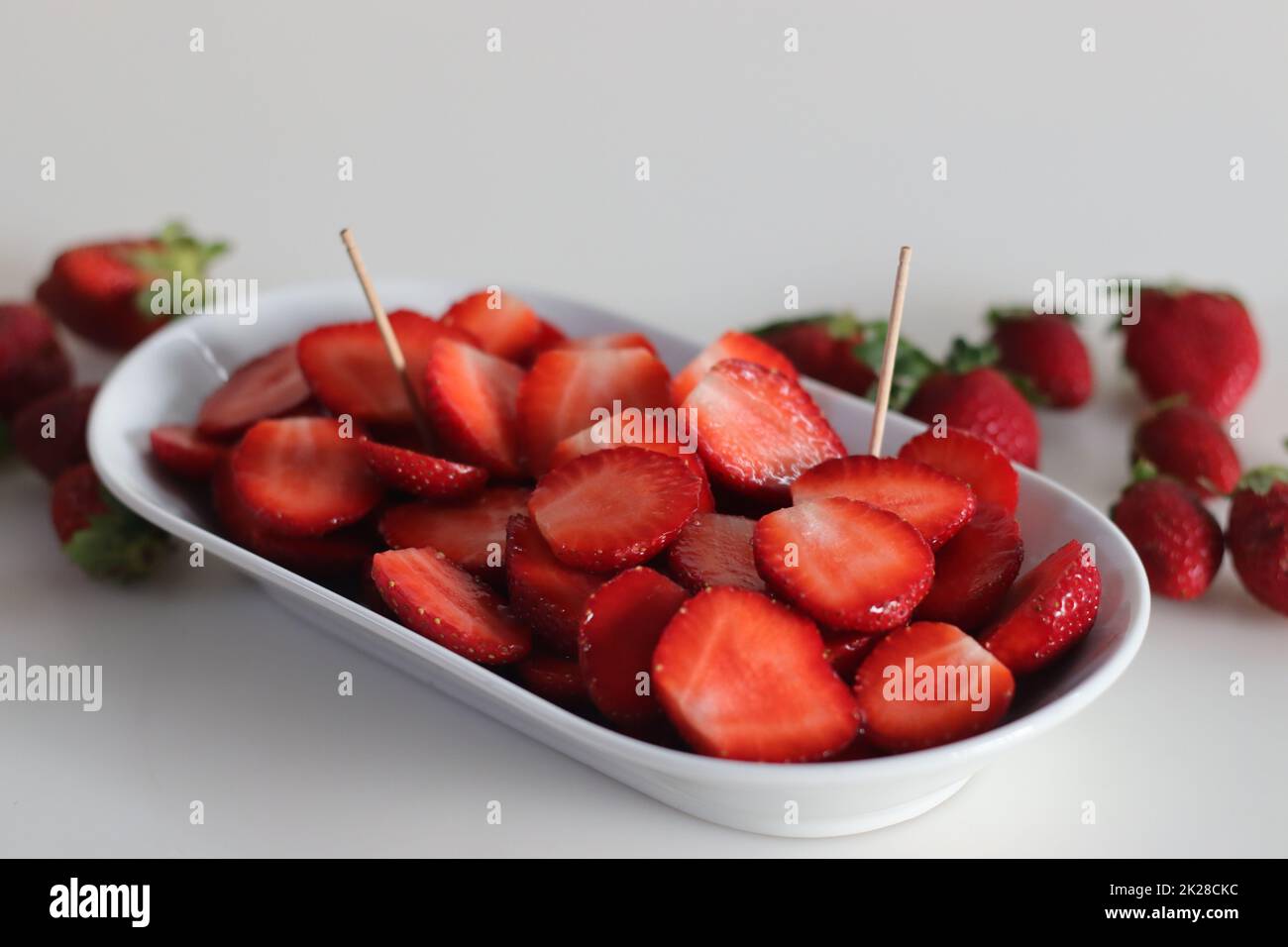 Half cut fresh strawberries inside a white bowl, shot on white ...