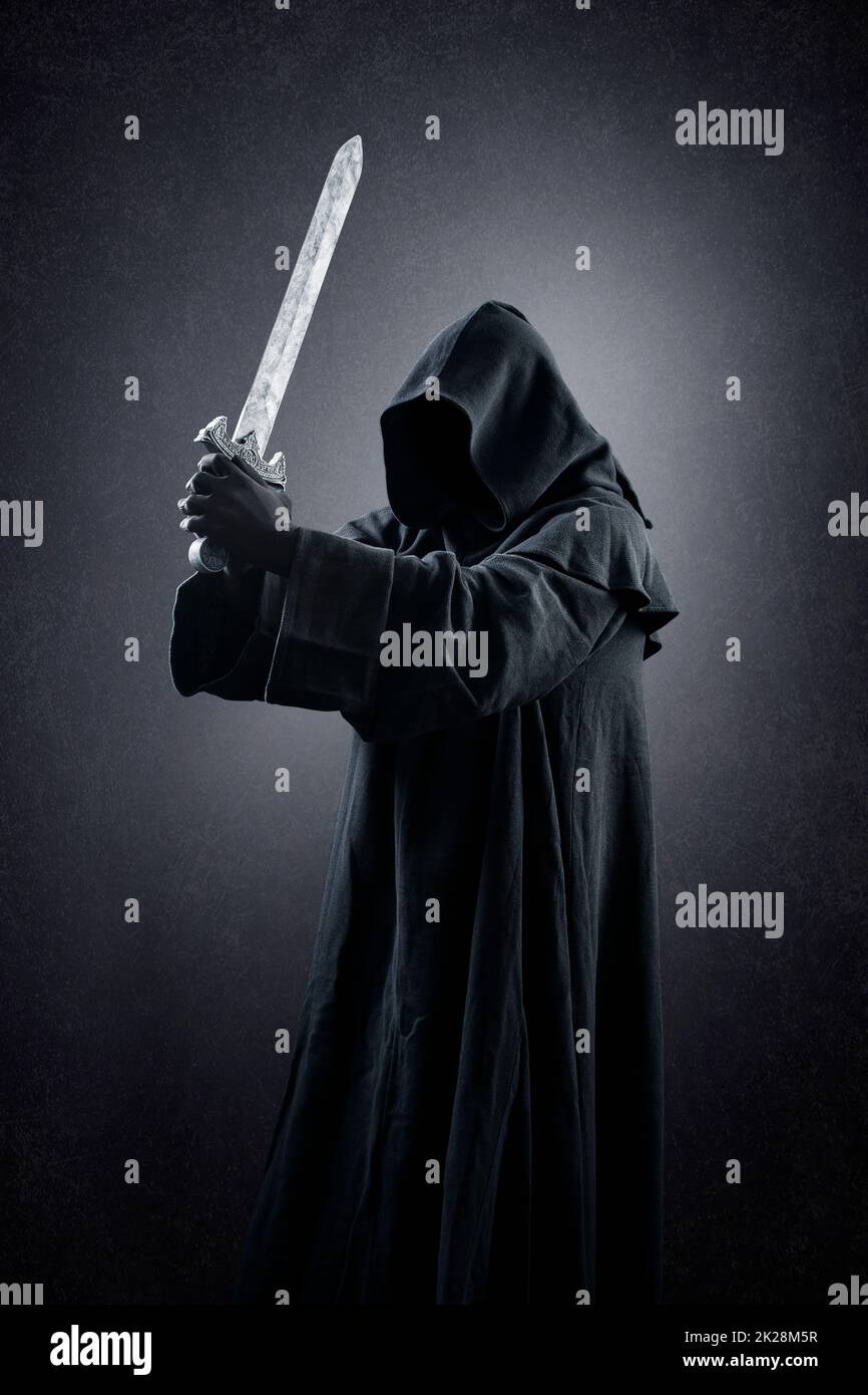 Warrior with hooded cape and medieval sword over dark misty background ...