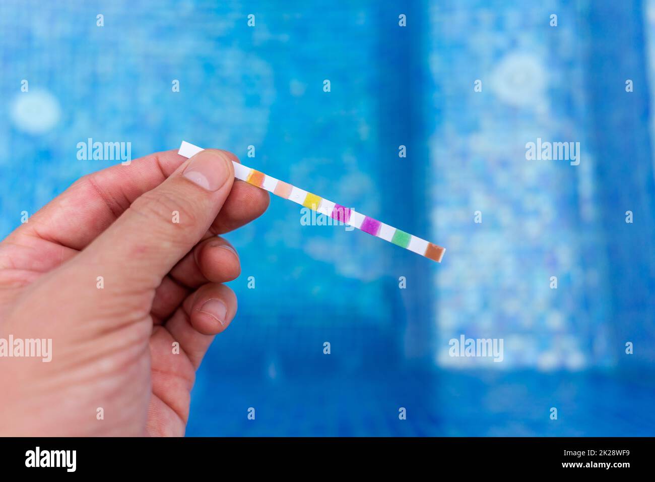 Hand with measuring pool strips to check water quality in a swimming ...