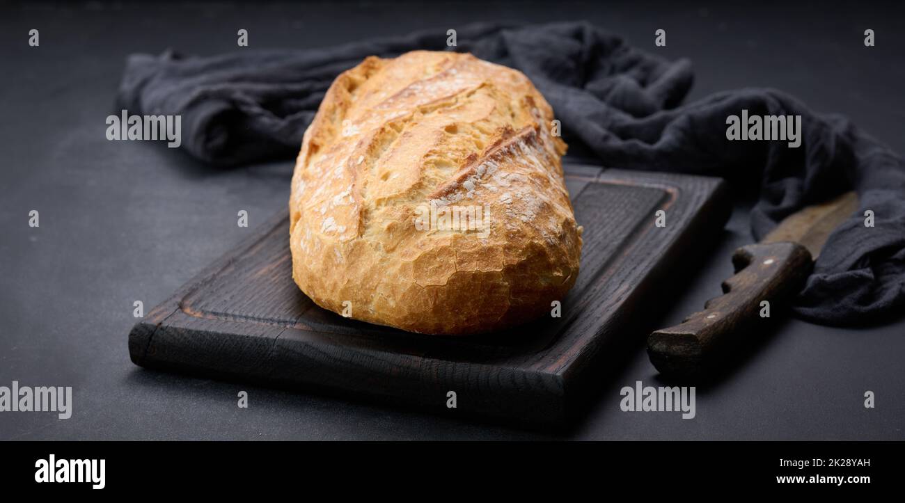 baked whole oval bread made from white wheat flour on a black table ...