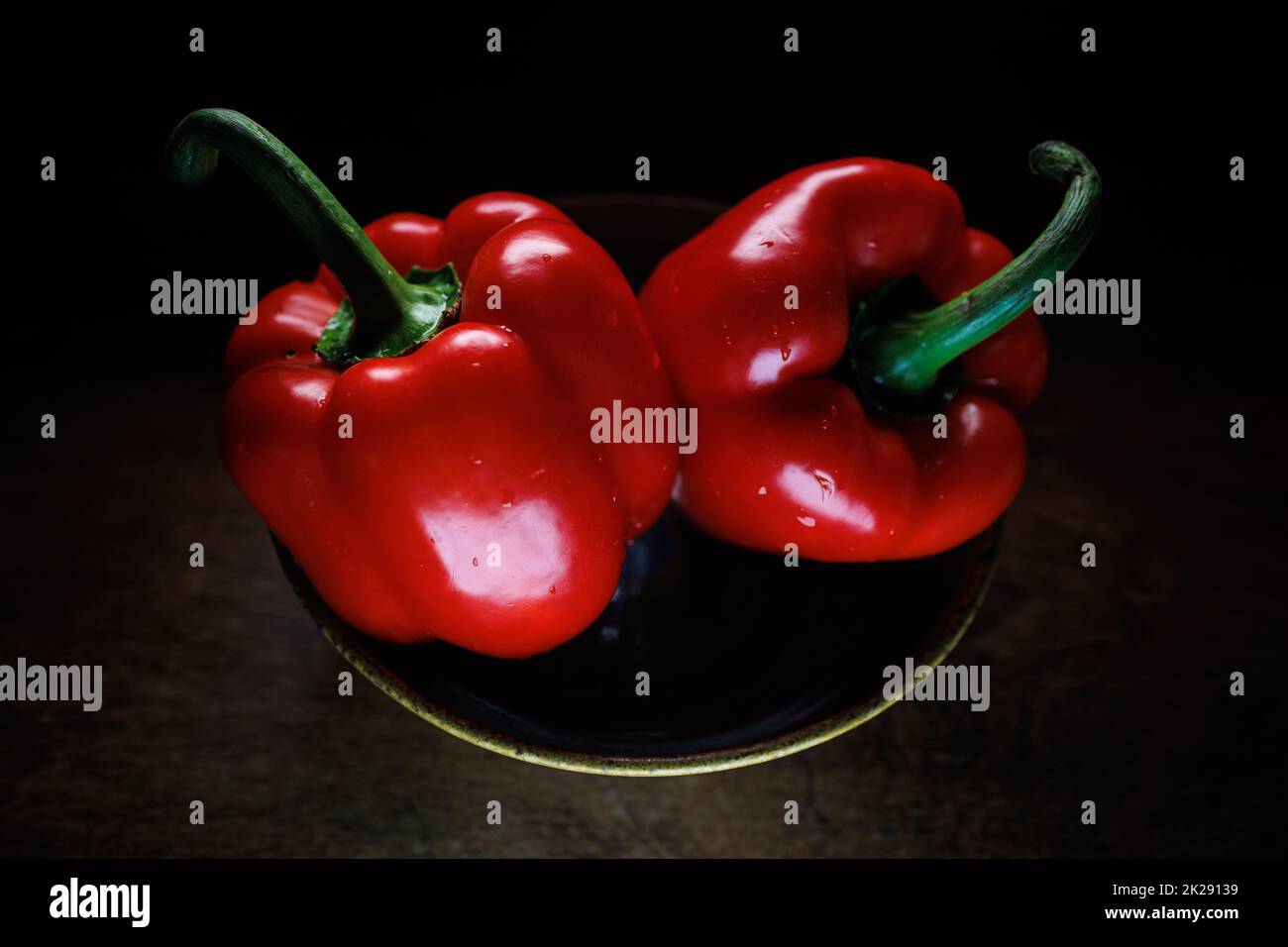 Two red pepper in bowl dark backround Stock Photo - Alamy