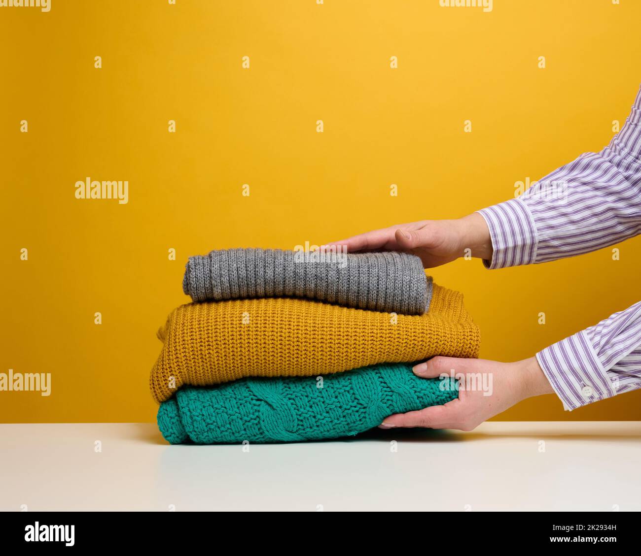 a woman holds a stack of washed folded things on a yellow background ...