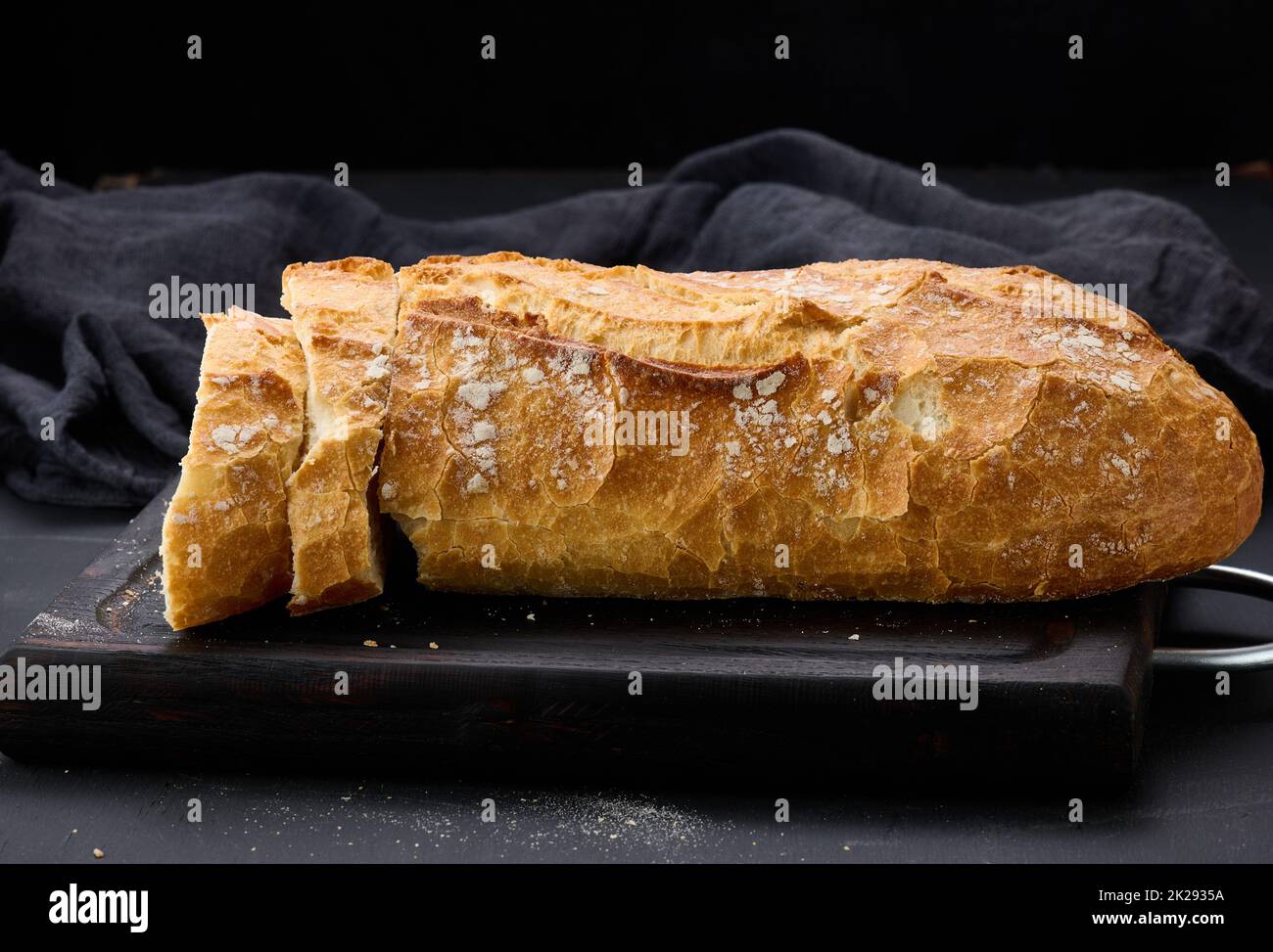 baked whole oval bread made from white wheat flour on a black table ...