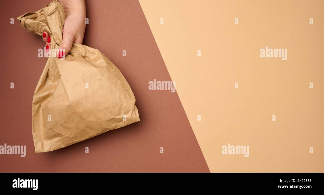hand holding a full paper bag of brown kraft paper ona brown background ...