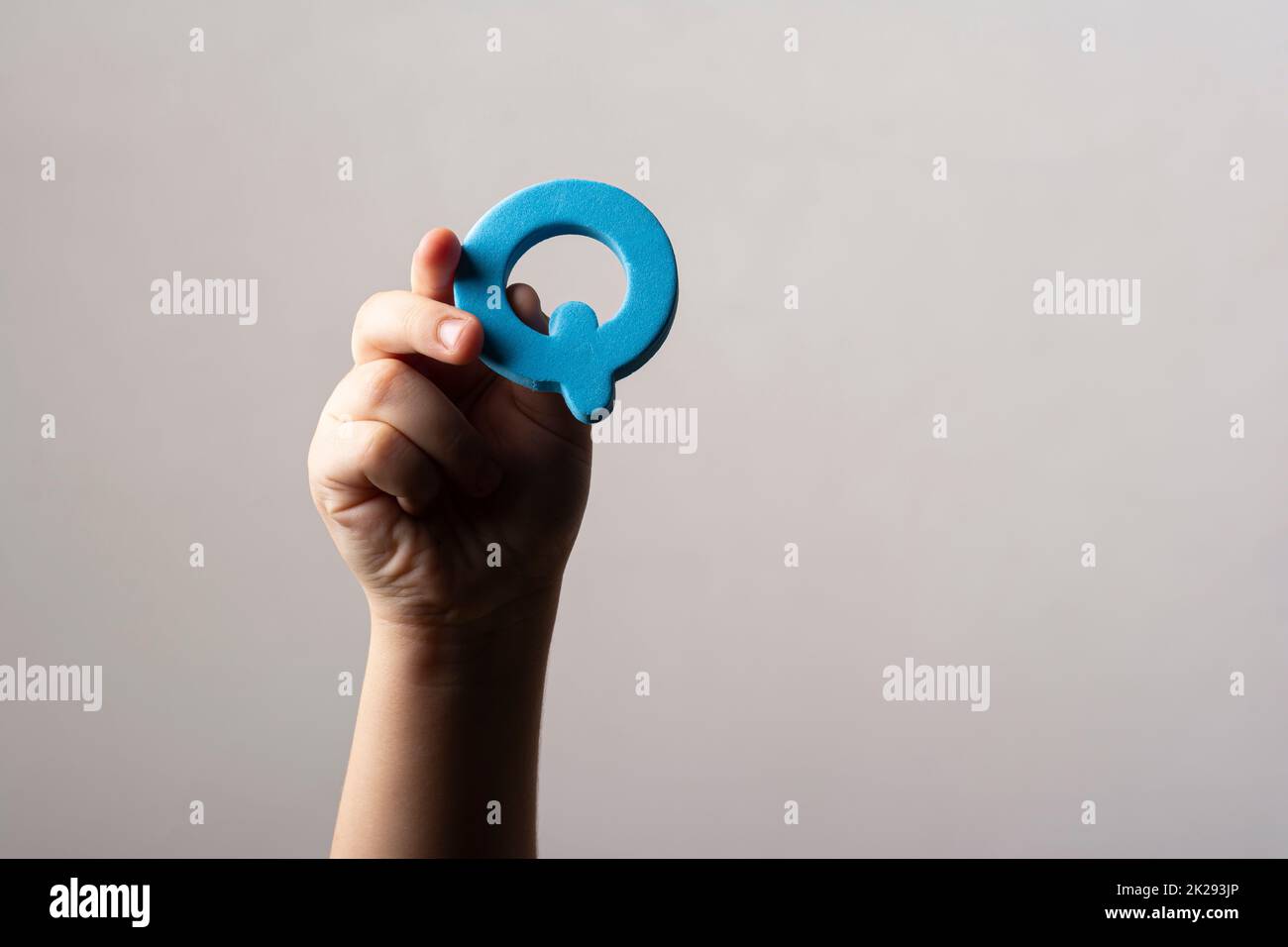 A child hand holding a spongy alphabet q letter in front of gray ...