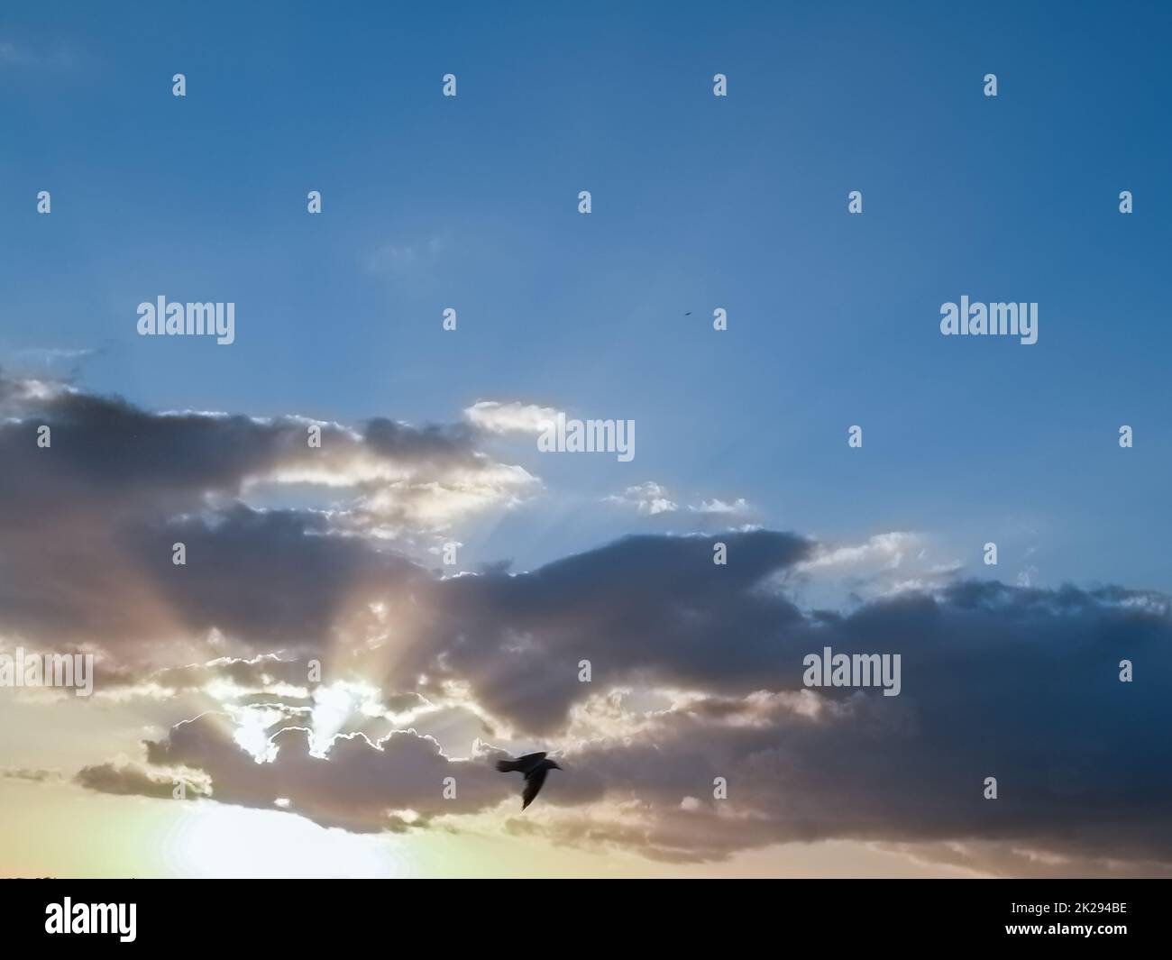 Sun rays burst out through clouds at sunrise under blue sky above Stock ...