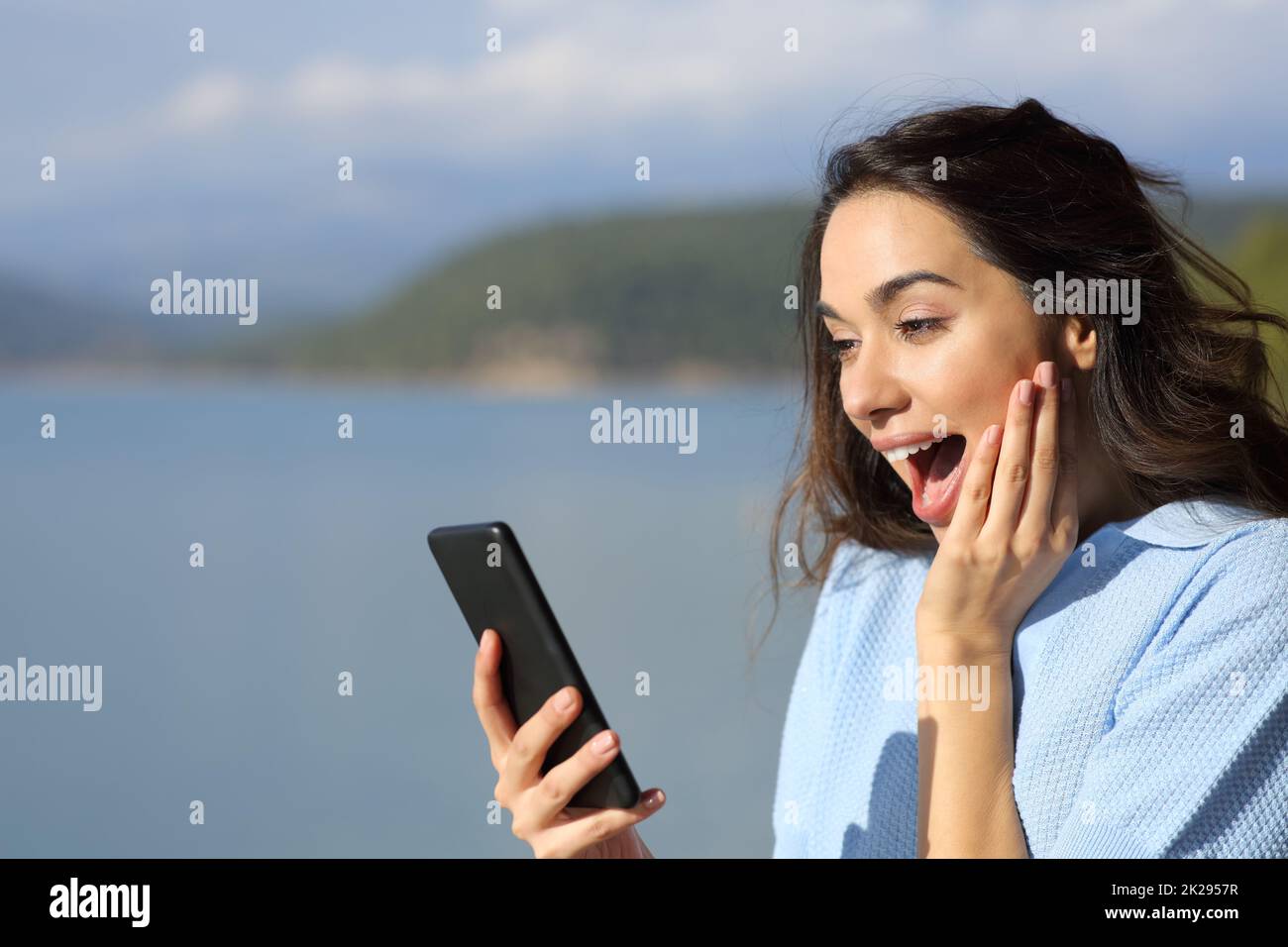 Amazed woman checking phone in a lake on holiday Stock Photo - Alamy