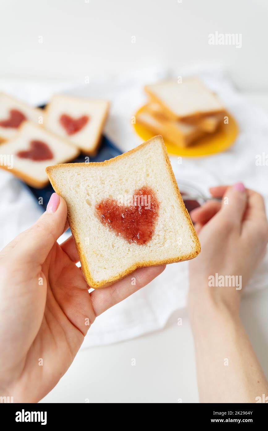 The girl makes a toast on which the heart is made of jam. Surprise ...
