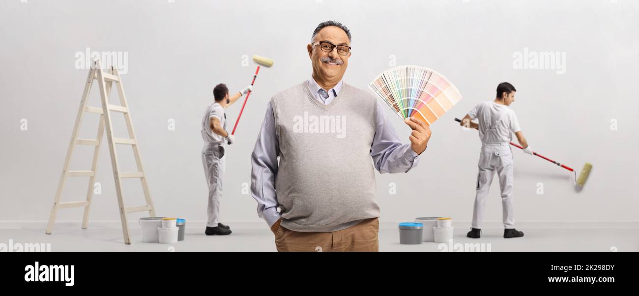 Mature man holding a color palette and painter working in the back ...