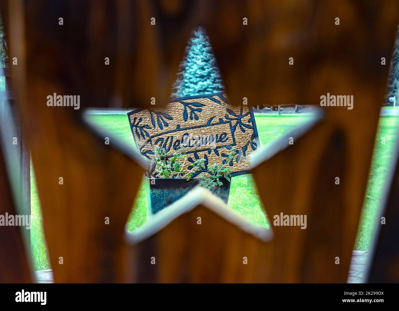 Here is a welcome sign as seen thru a star shape and slats of a pine ...