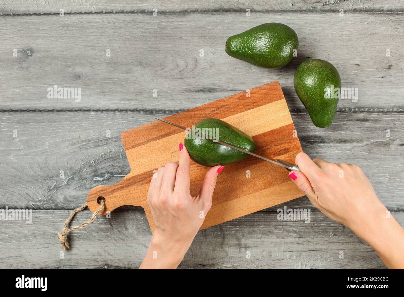 Tabletop view, woman hands holding chef knife, cutting avocado on ...