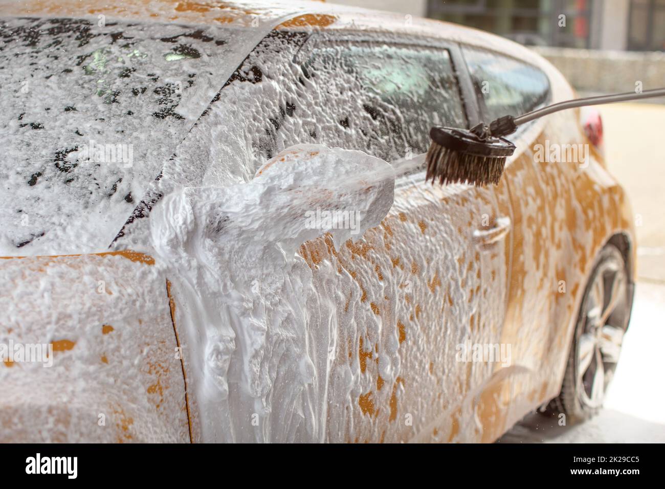 Yellow car washed in self service carwash. Shampoo spraying to side ...