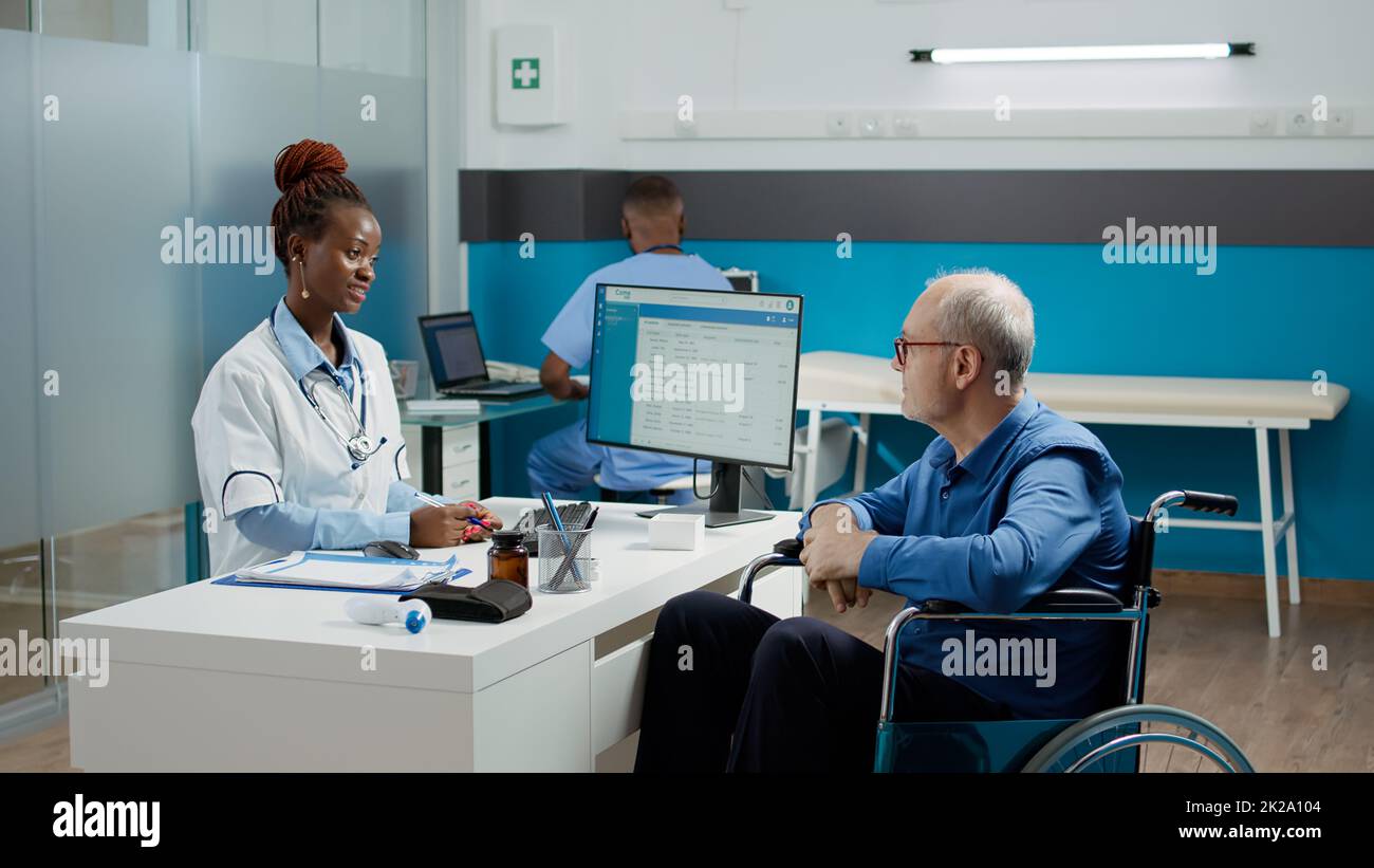 General practitioner doing checkup visit with patient in wheelchair ...