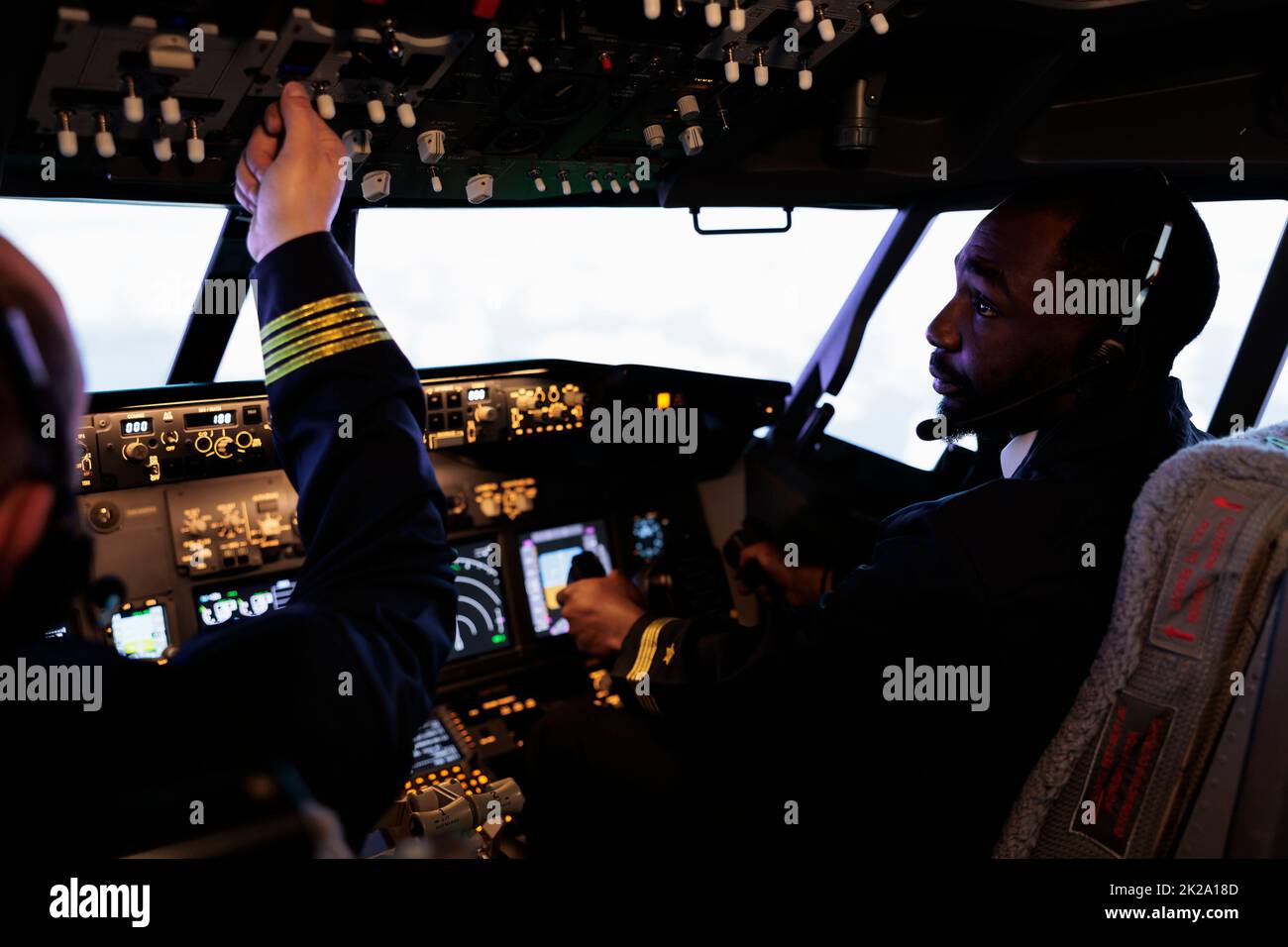 Multiethnic team of pilots using control panel in cockpit to fly ...