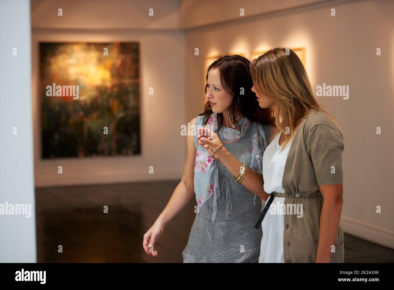 Appreciating art. Two young woman examining a painting up close while ...