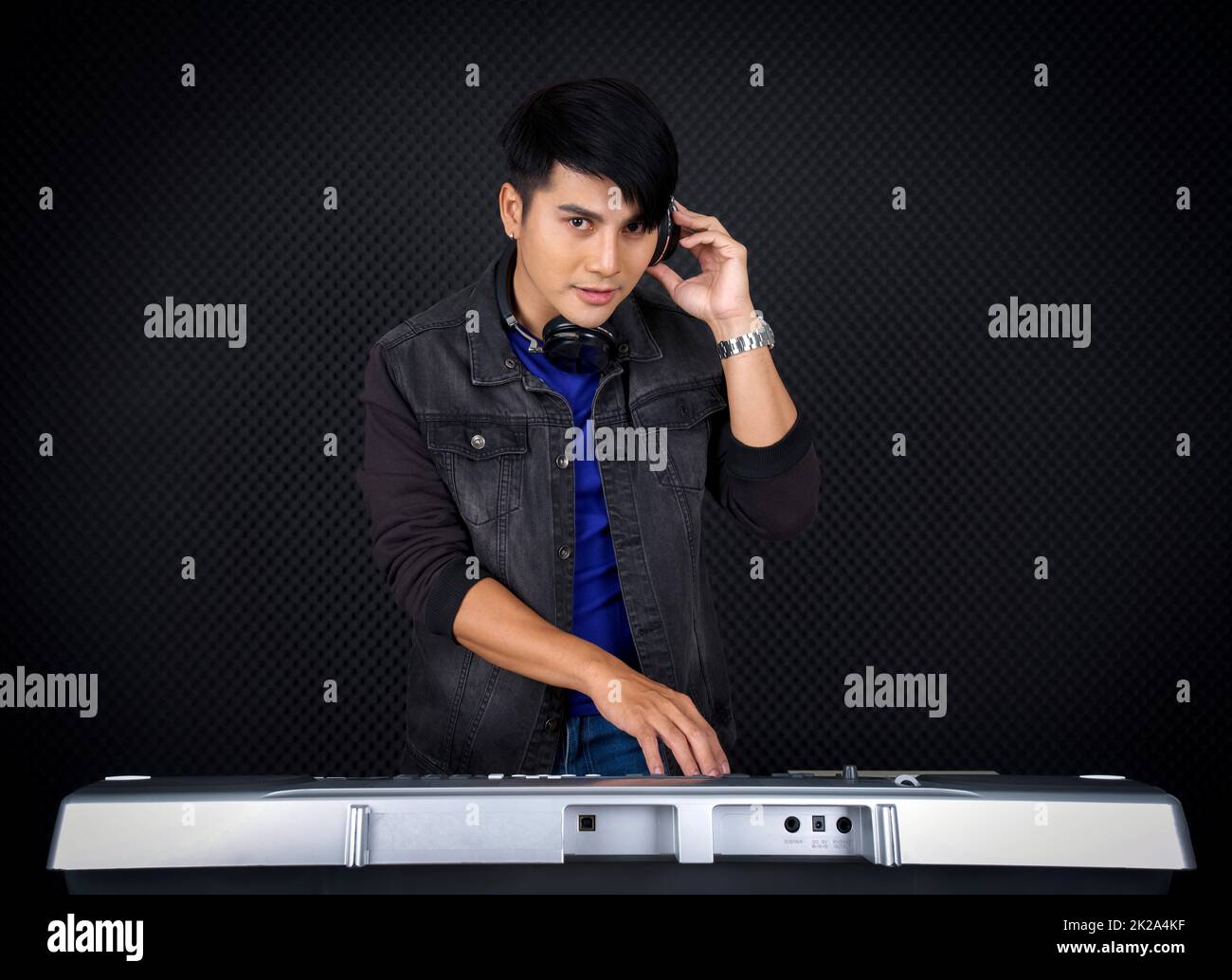 Young asian man with headphones playing an electric keyboard in front ...