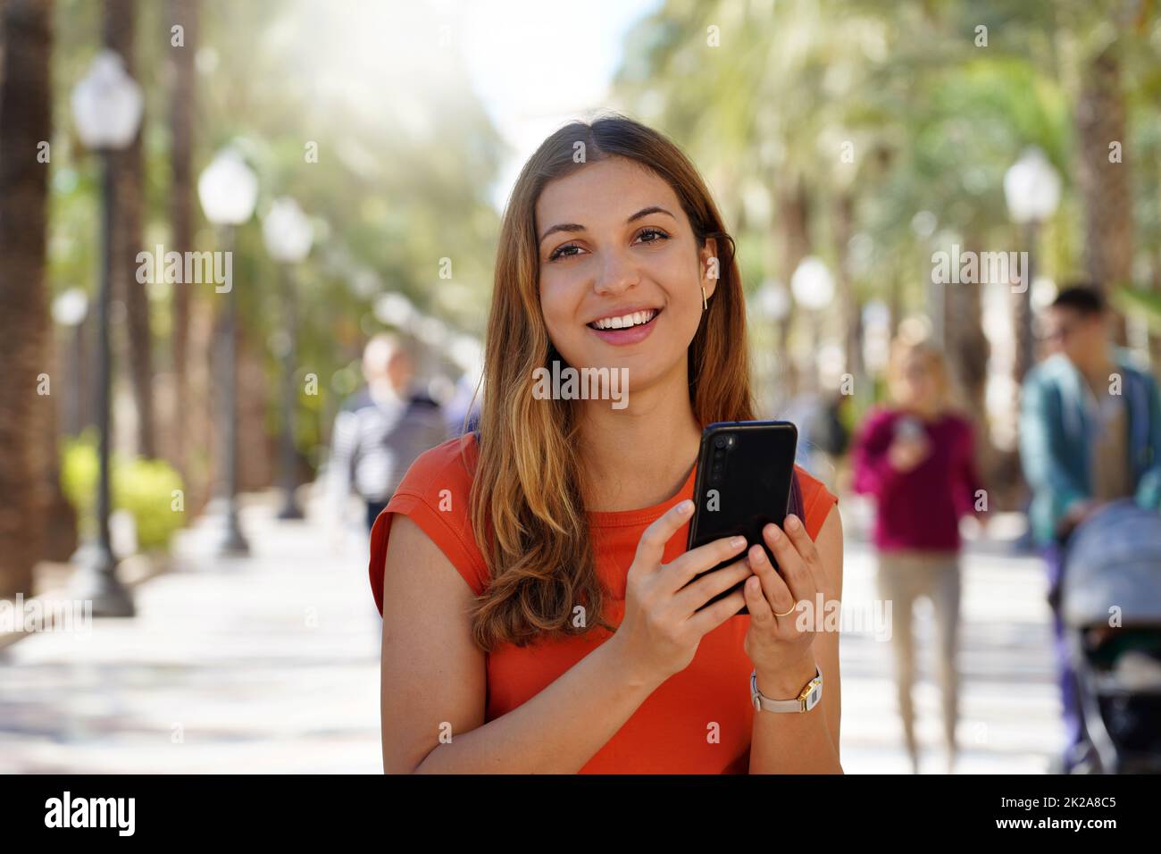 Young hispanic girl smiling happy using smartphone at the esplanade of ...
