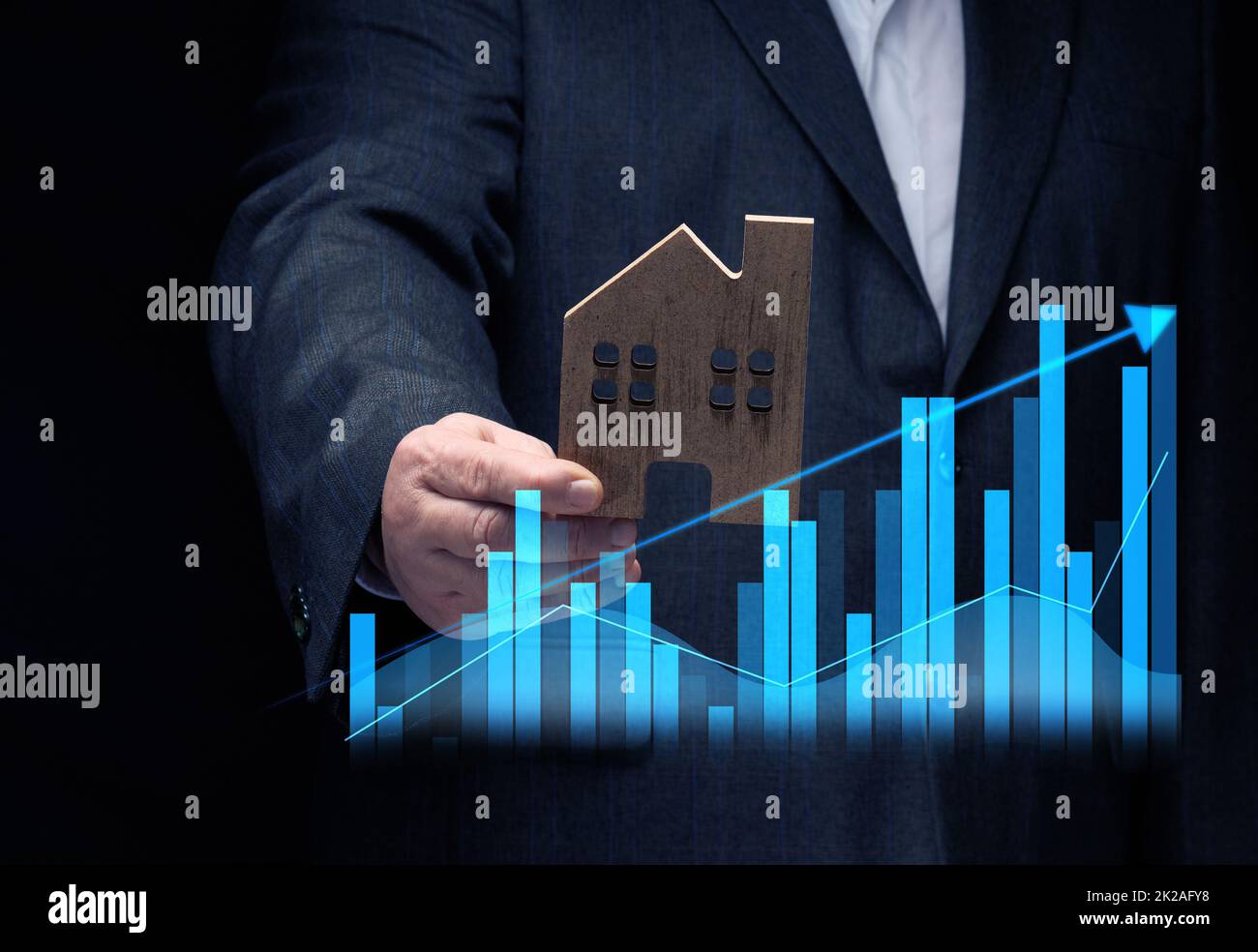 hand holds a wooden model of a house on a dark background. Real estate ...
