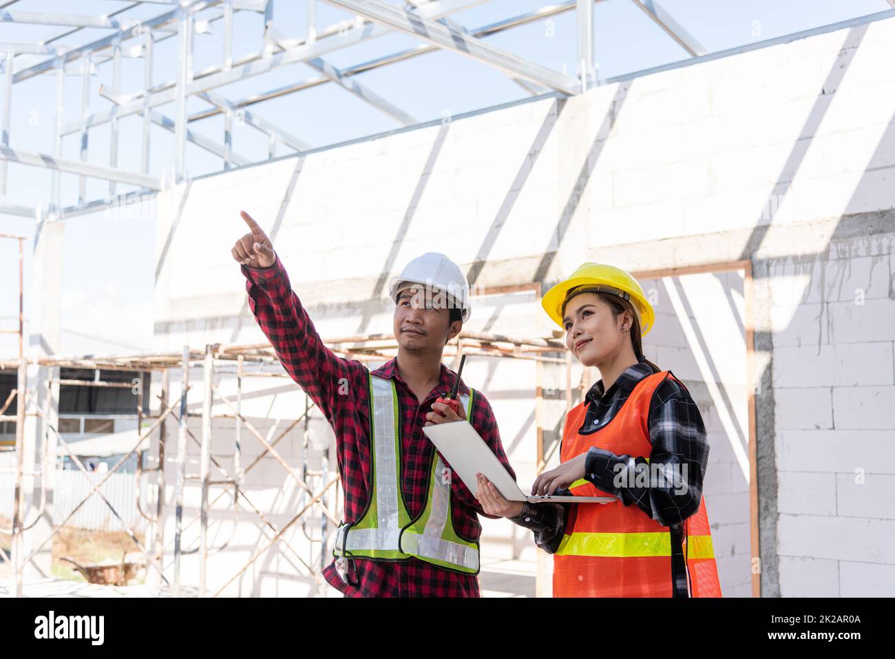 Asian engineer foreman worker man and woman working at building construction site use laptop and ...