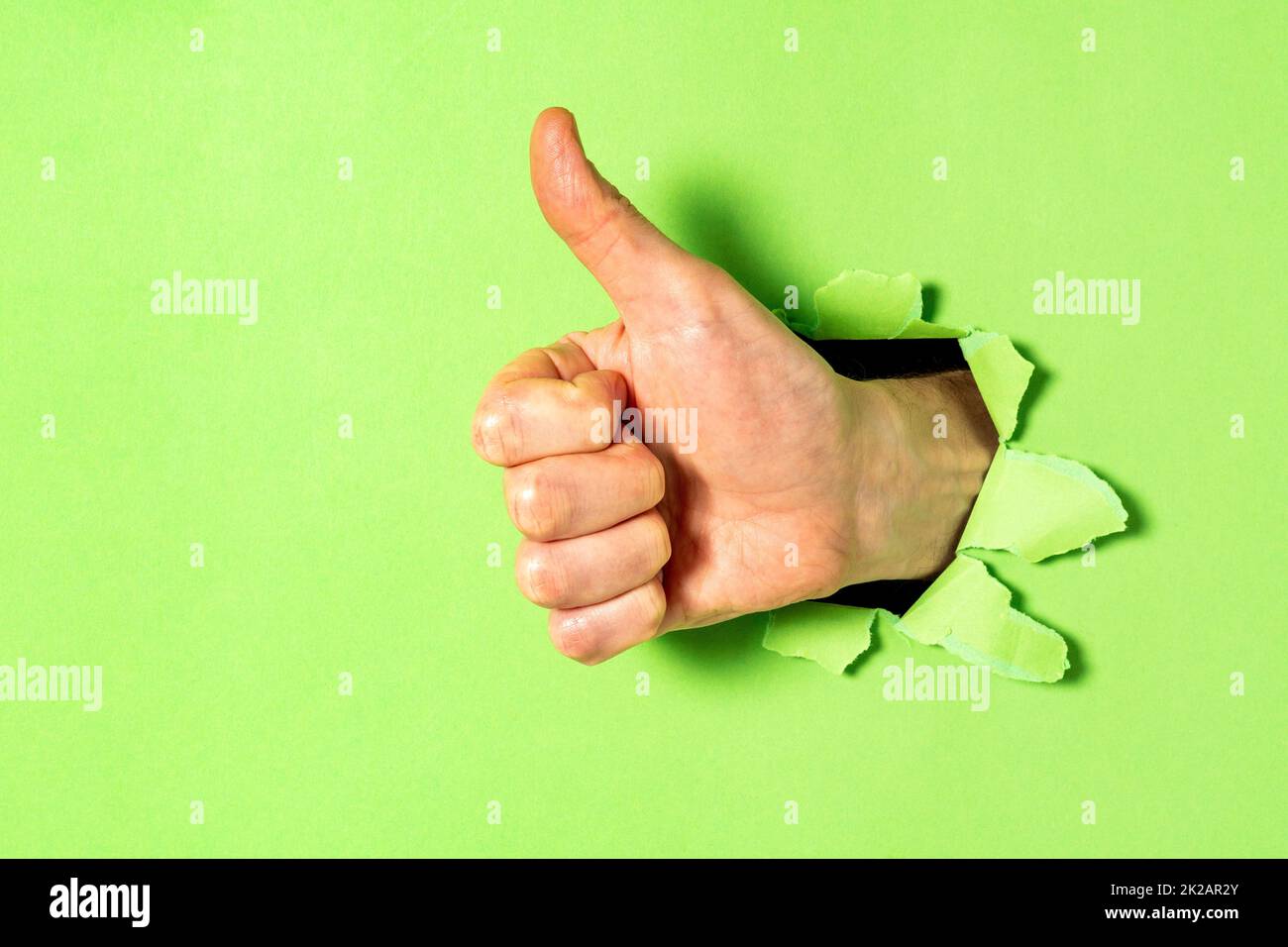 Hand with thumb up gesture through hole in green paper wall Stock Photo ...