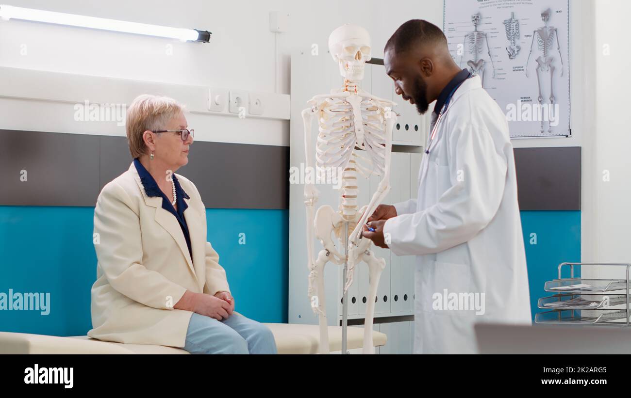 Male osteopath examining human skeleton bones to senior woman ...