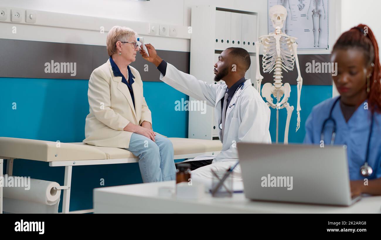 General practitioner using thermometer to check temperature on senior ...