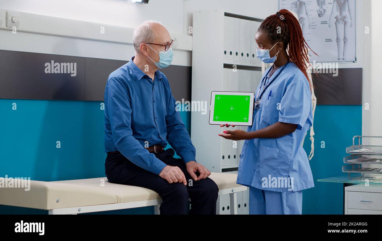 Nurse showing tablet with greenscreen display to senior man in medical ...