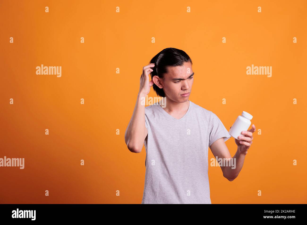 Asian young man confused about what pills to take, looking at tablets ...
