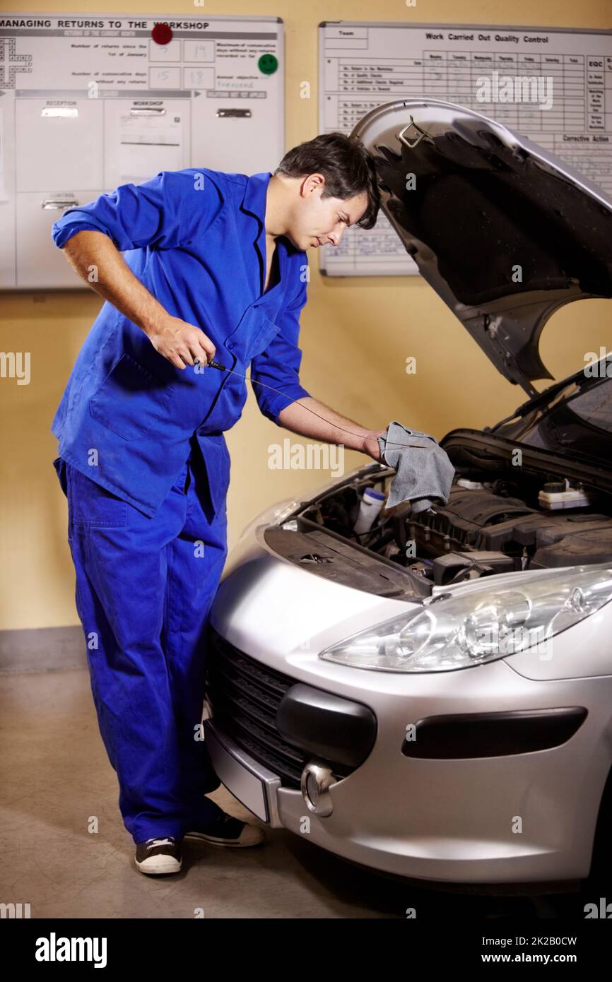 The oil seems to be fine. A male mechanic wiping off the oil stick to ...