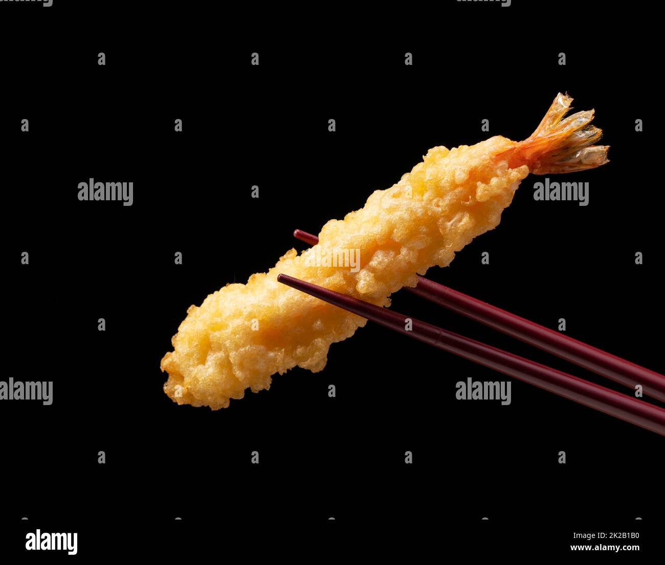 Shrimp tempura lifted with chopsticks against a black background Stock ...