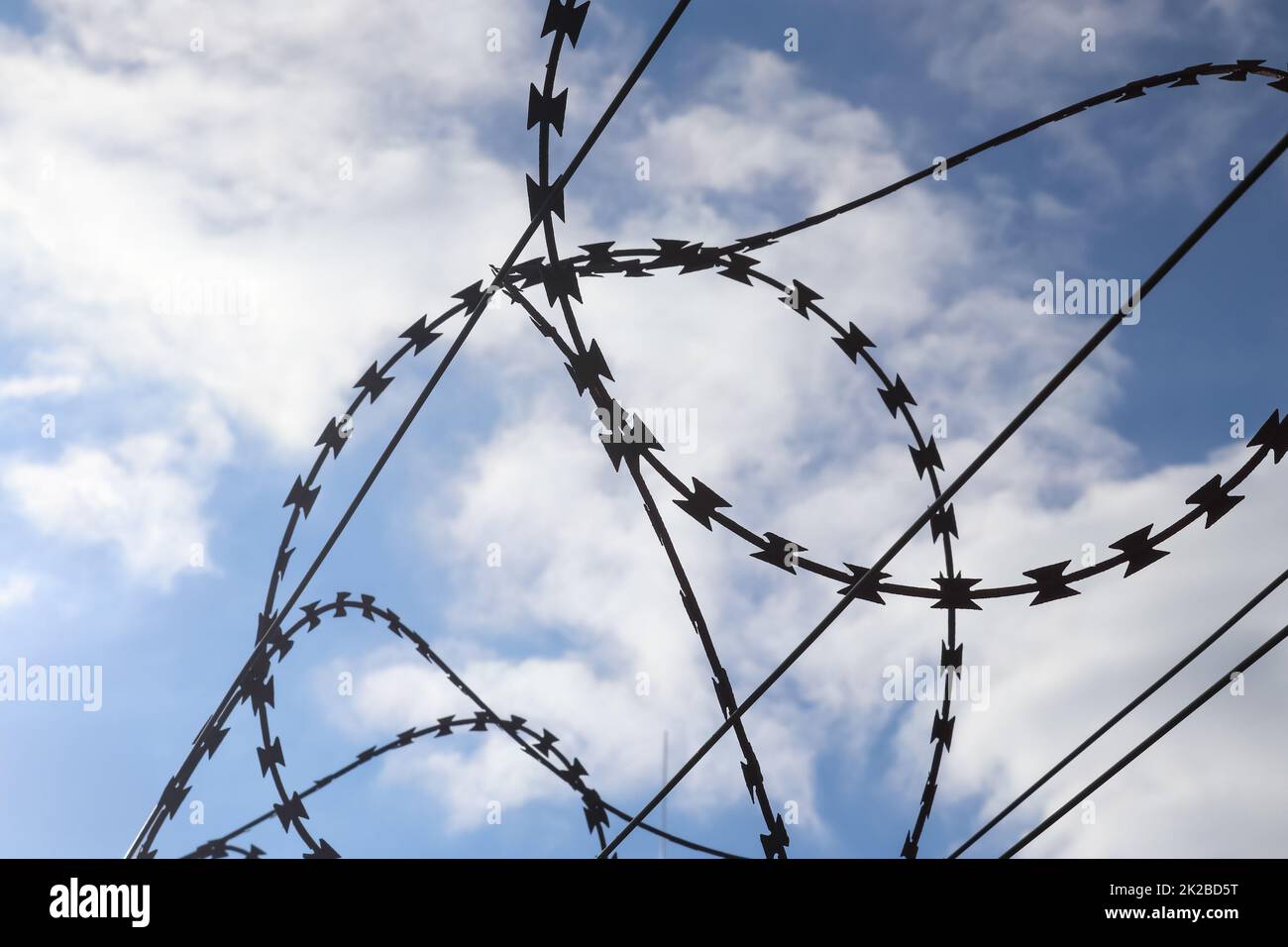 Barbed wire against a cloudy sky on a big fence at a border Stock Photo ...