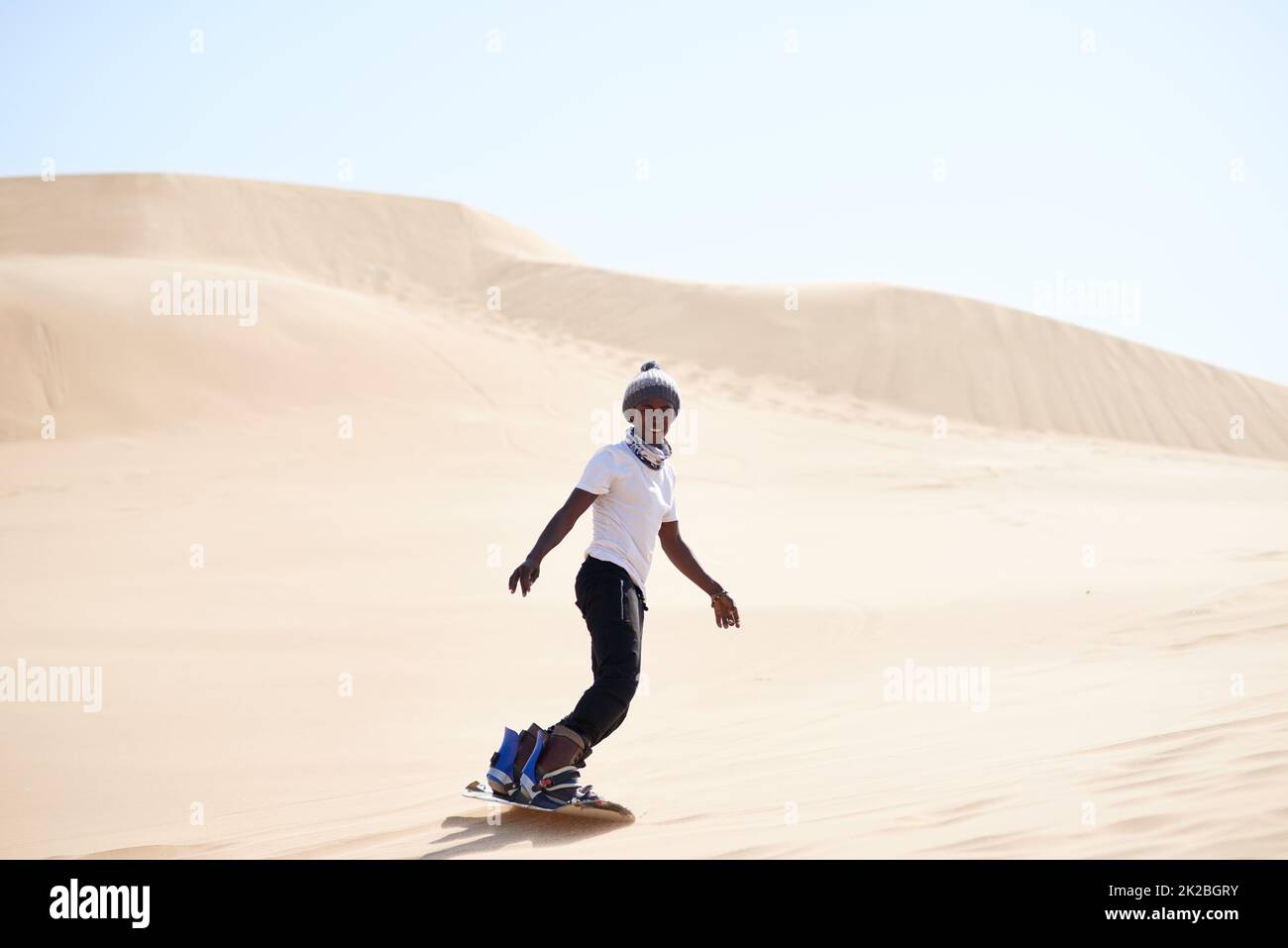 Lets shred the sand. Portrait of a young man sandboarding in the desert ...