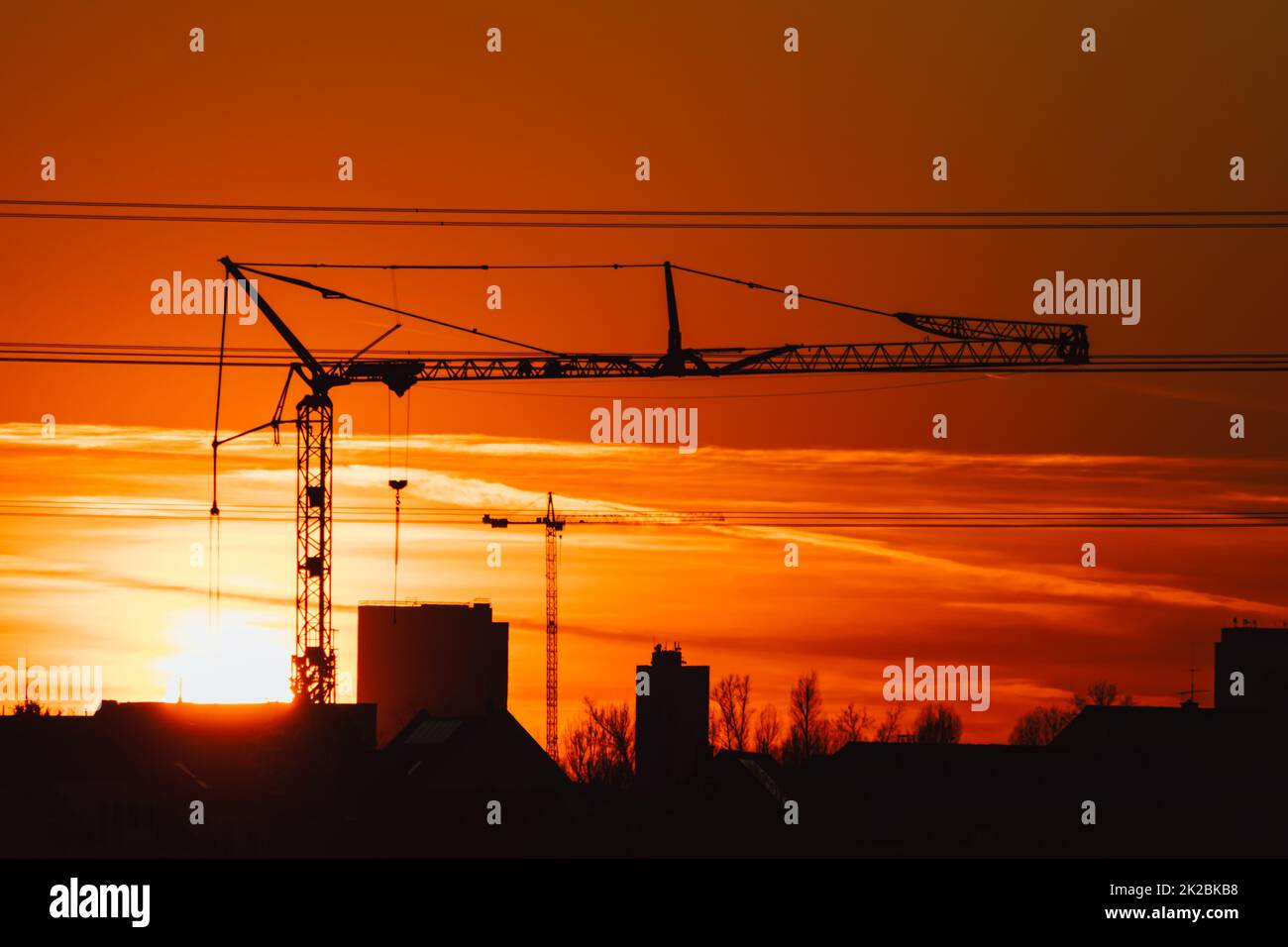 Tall construction crane silhouette in orange sky sunset shows ...