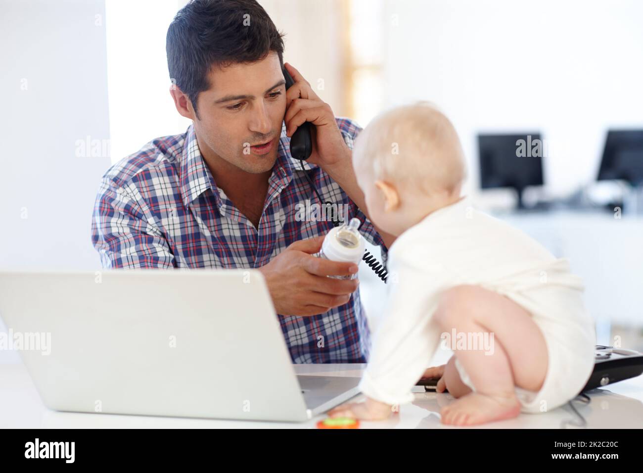 Extreme multi-tasking. Shot of a working dad giving his baby a bottle ...