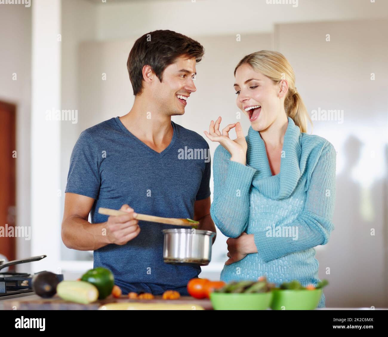 Perfecto. Shot of a handsome young man giving his wife a taste of his ...