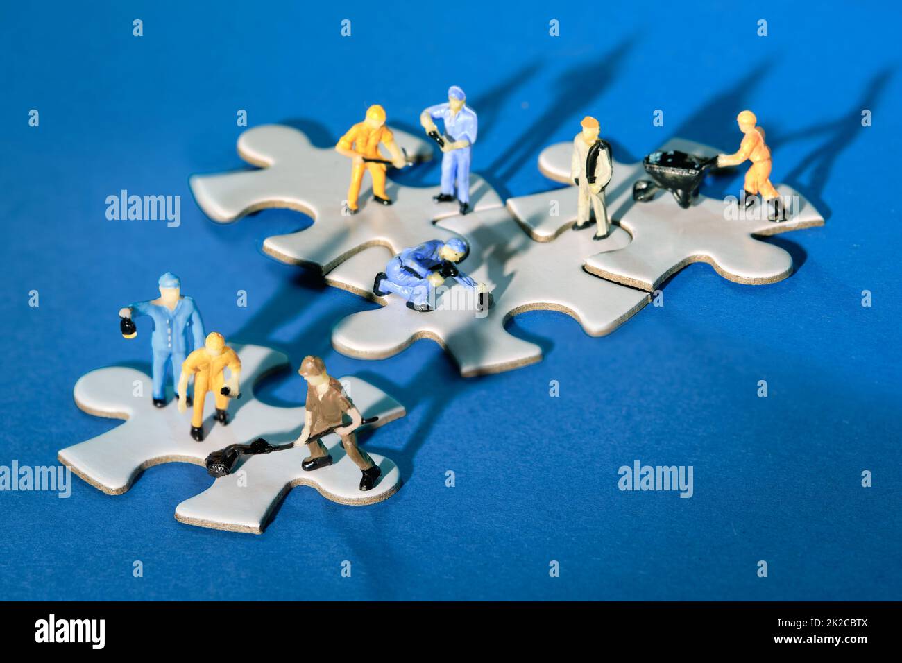 Team of tiny worker miniature figures on linked jigsaw puzzle pieces ...